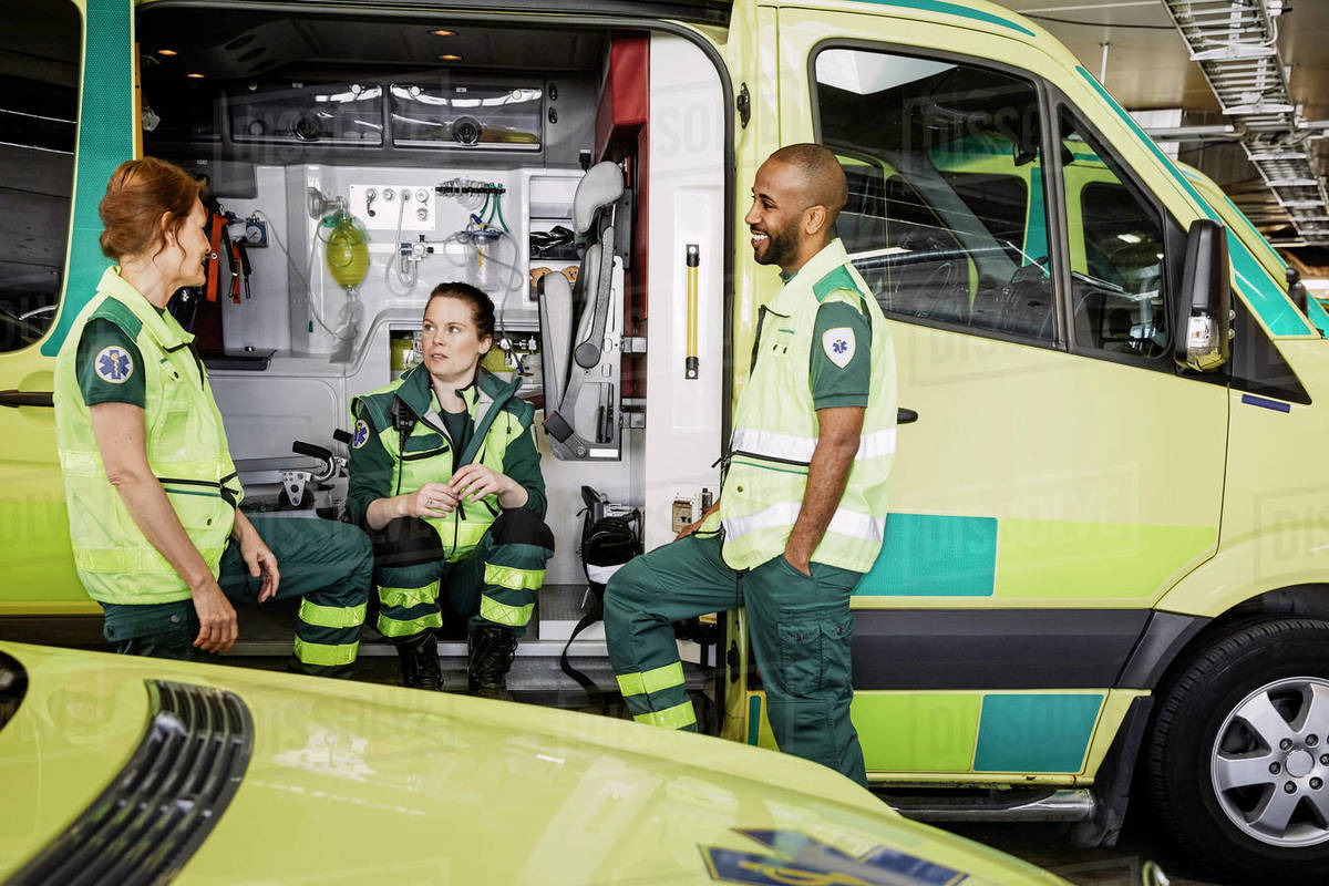 Male and female paramedics talking while sitting in ambulance at ...
