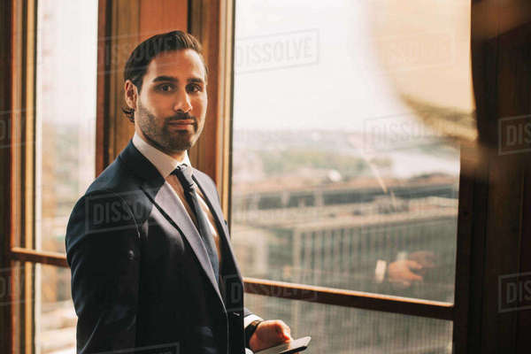 Portrait of confident male advisor standing by window at legal office ...