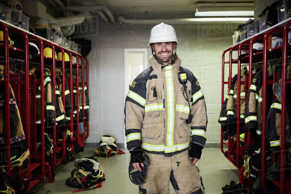 Portrait of smiling male firefighter standing in locker room at fire ...
