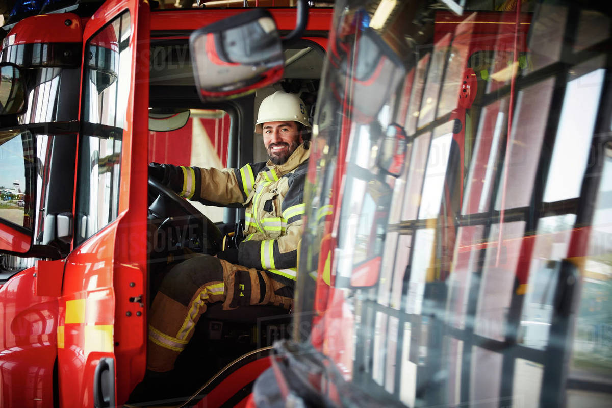 Portrait of smiling male firefighter sitting in fire truck at fire ...