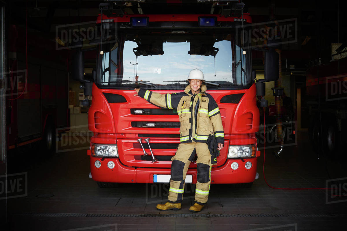 Full length portrait of smiling female firefighter standing in front of ...