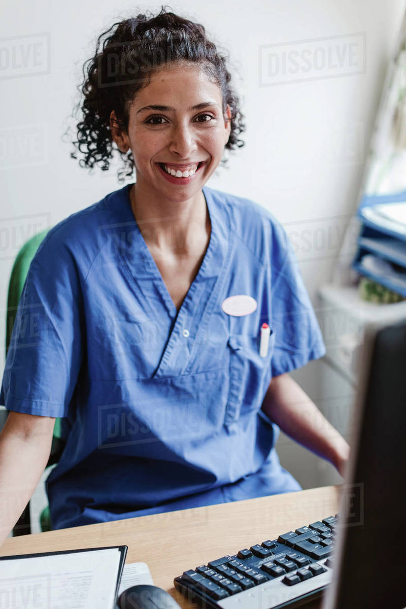 Portrait of smiling female nurse sitting at desk in hospital - Royalty ...