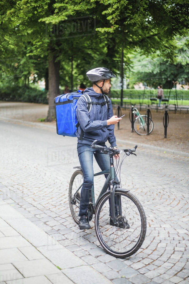 Full length of food delivery man on bicycle at street - Royalty-free ...