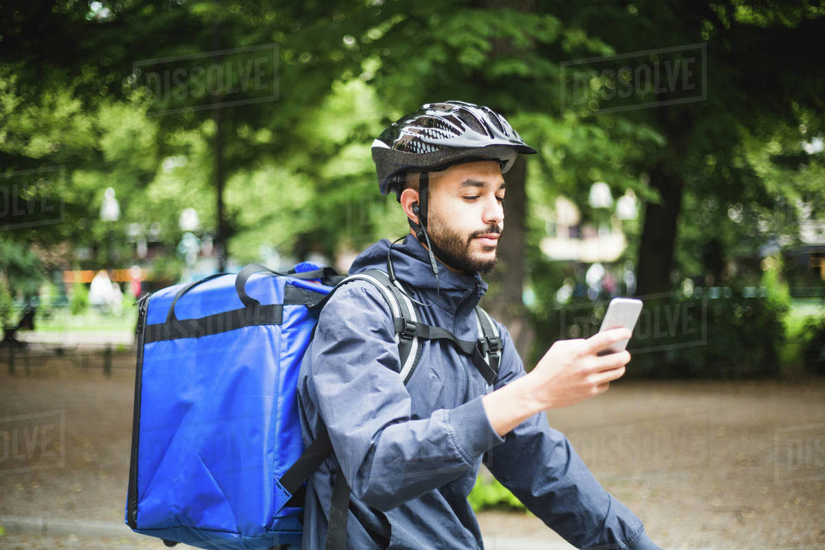 Food delivery man using smart phone on street in city - Royalty-free ...