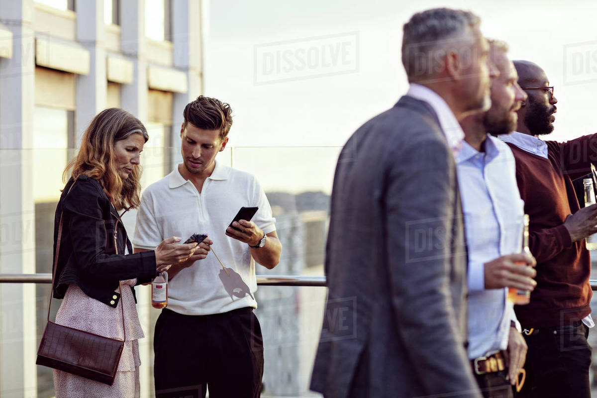 Professionals talking over smart phones while colleagues enjoying in ...