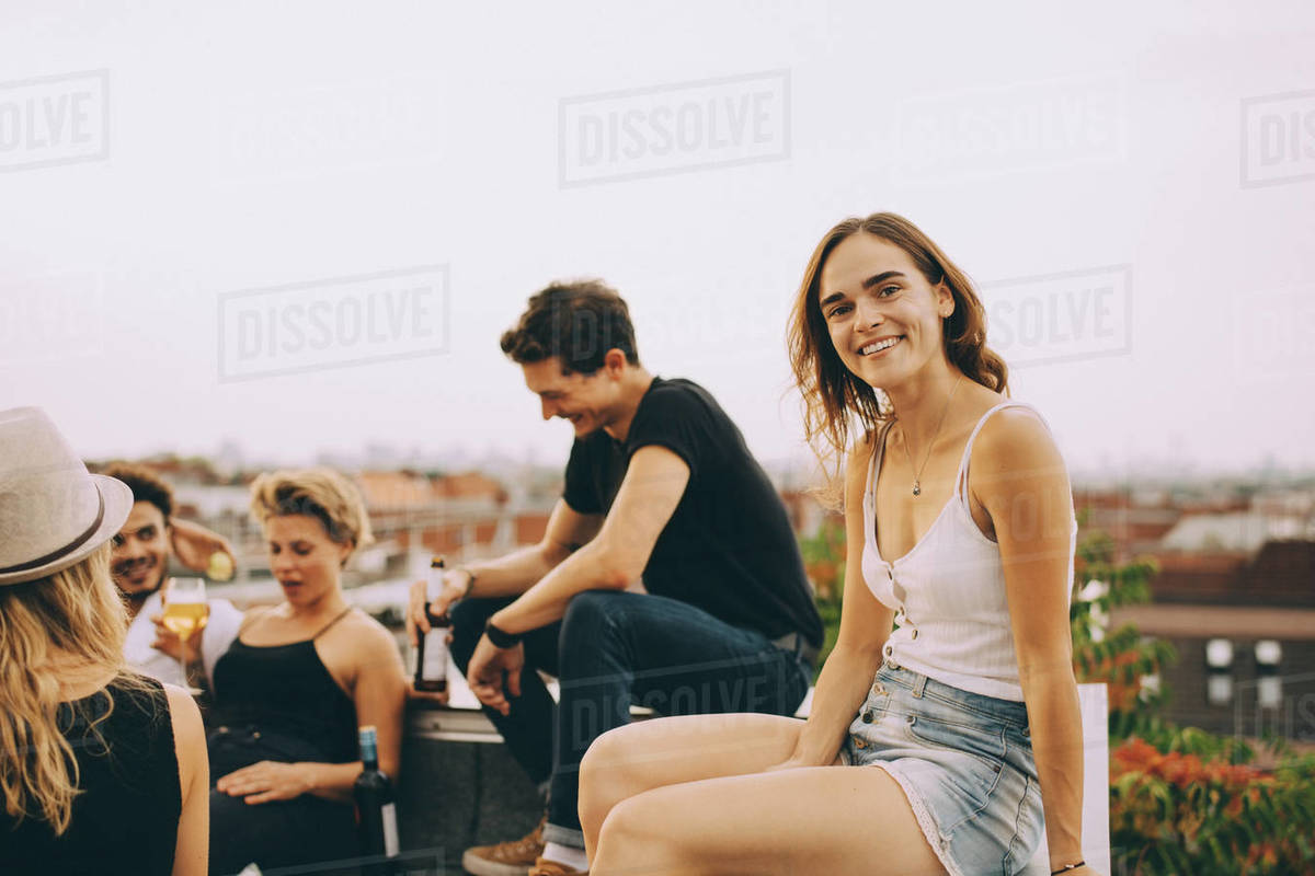 Smiling young woman sitting with friends at rooftop party - Royalty ...