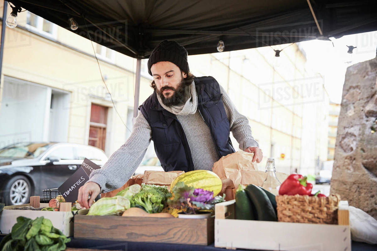 Male vendor arranging vegetables while standing at market stall ...