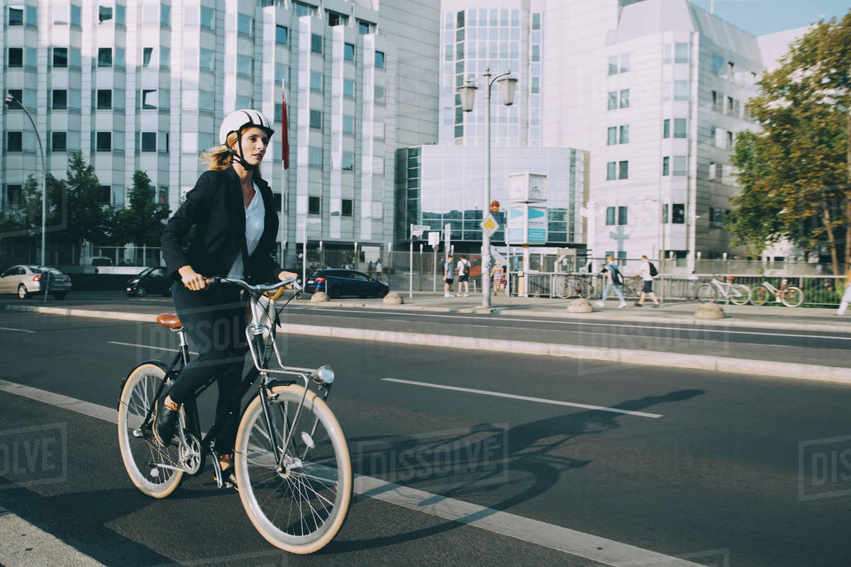 Full length of young woman wearing helmet riding bicycle on street in ...