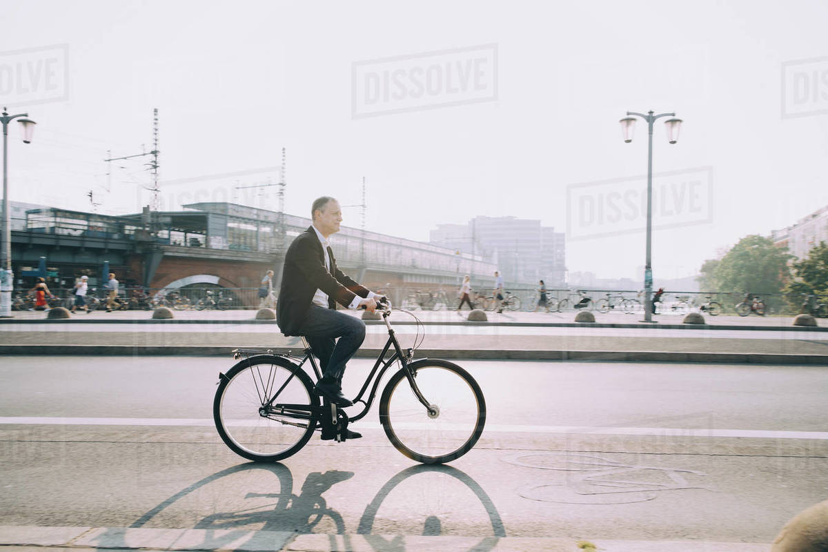 Side view of male entrepreneur riding bicycle on city street against ...
