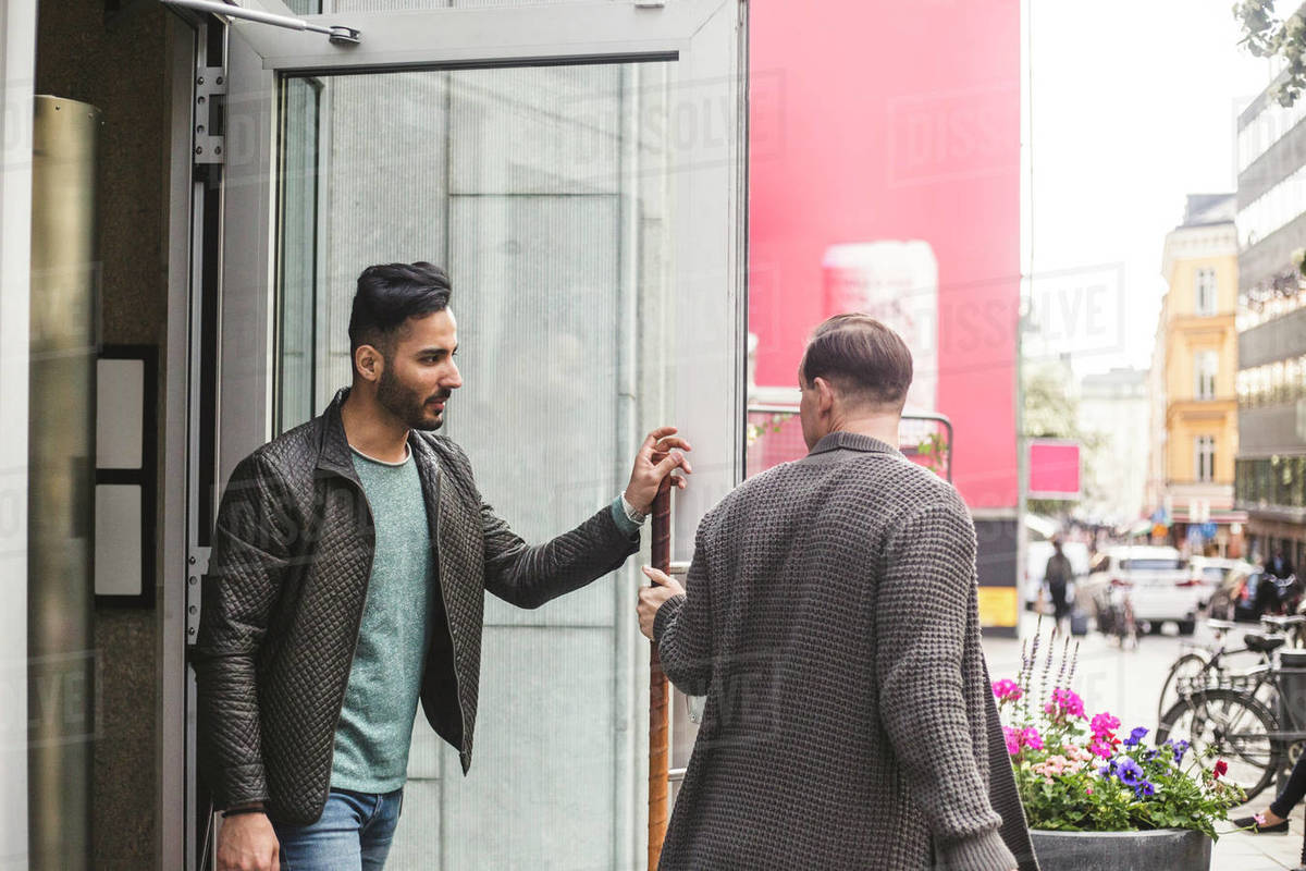 Young businessman walking out of building with coworker at entrance in ...