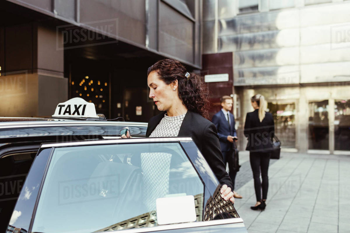 Female entrepreneur entering in taxi while coworkers standing in ...