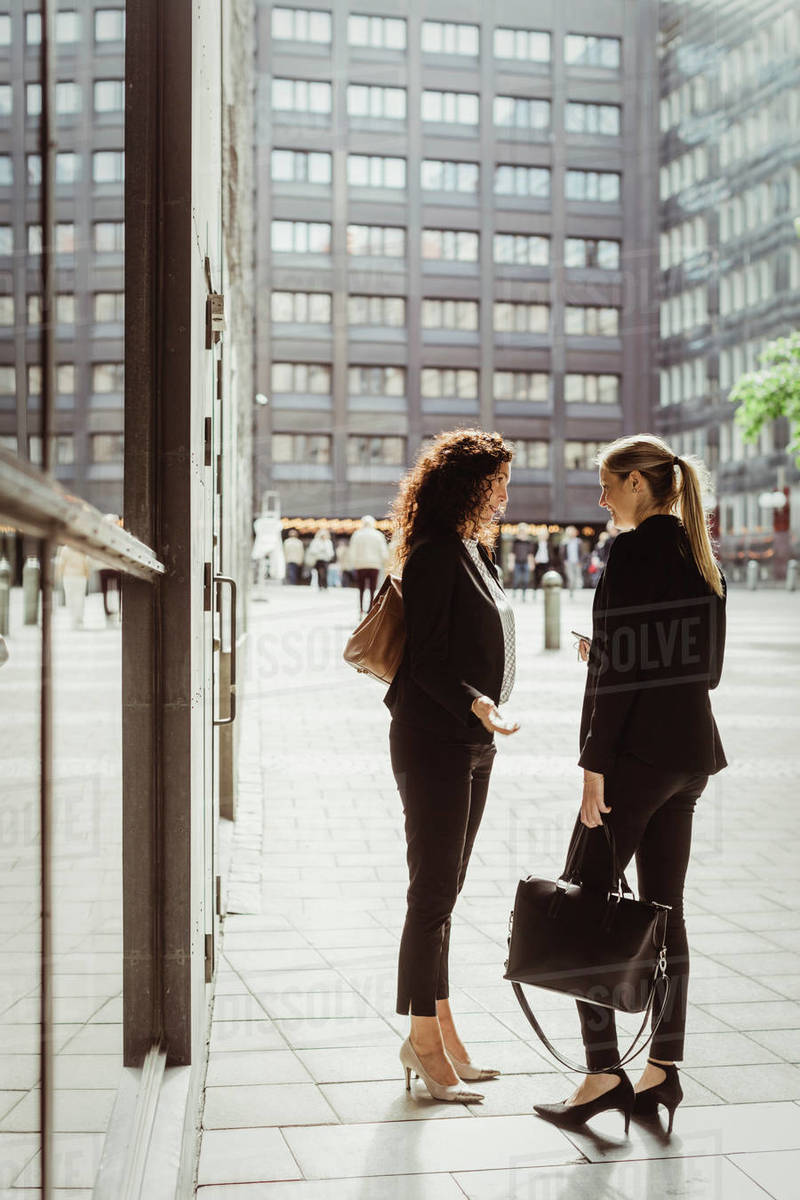 Businesswomen talking while standing by building - Royalty-free Stock ...