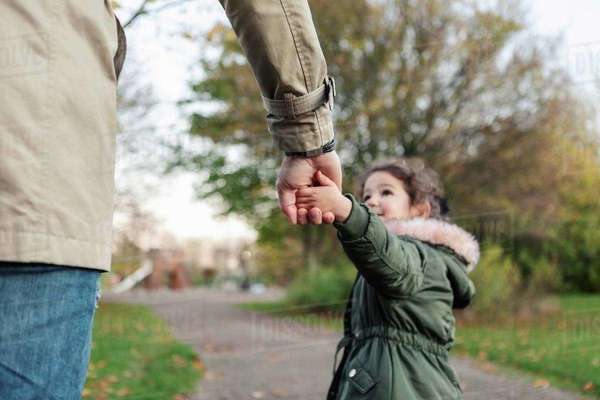 Daughter pulling father while holding hands in park during autumn ...