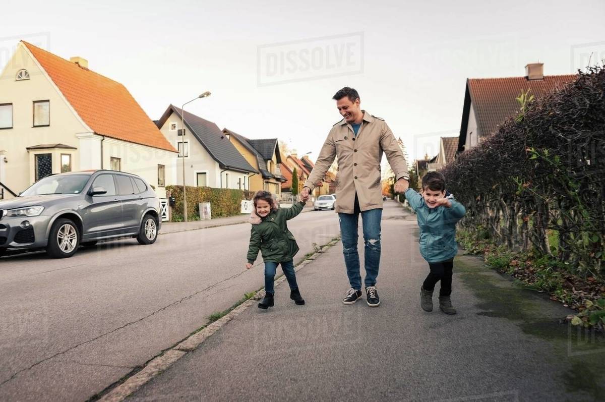 Smiling father walking with children on sidewalk during autumn ...