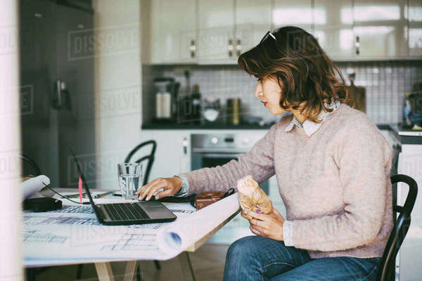 Woman in kitchen working from home having lunch - Stock Photo - Dissolve