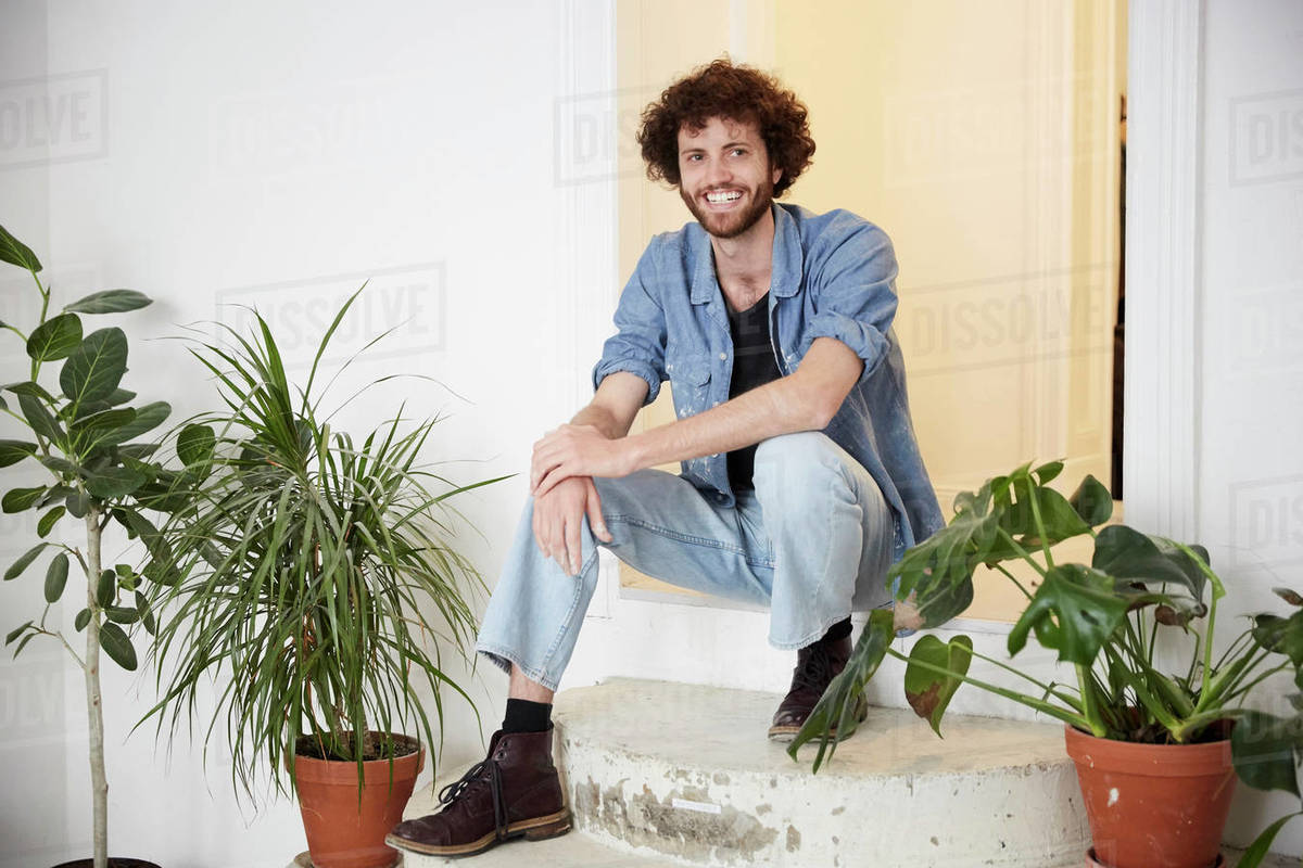 Full length portrait of smiling man sitting at entrance of art class ...