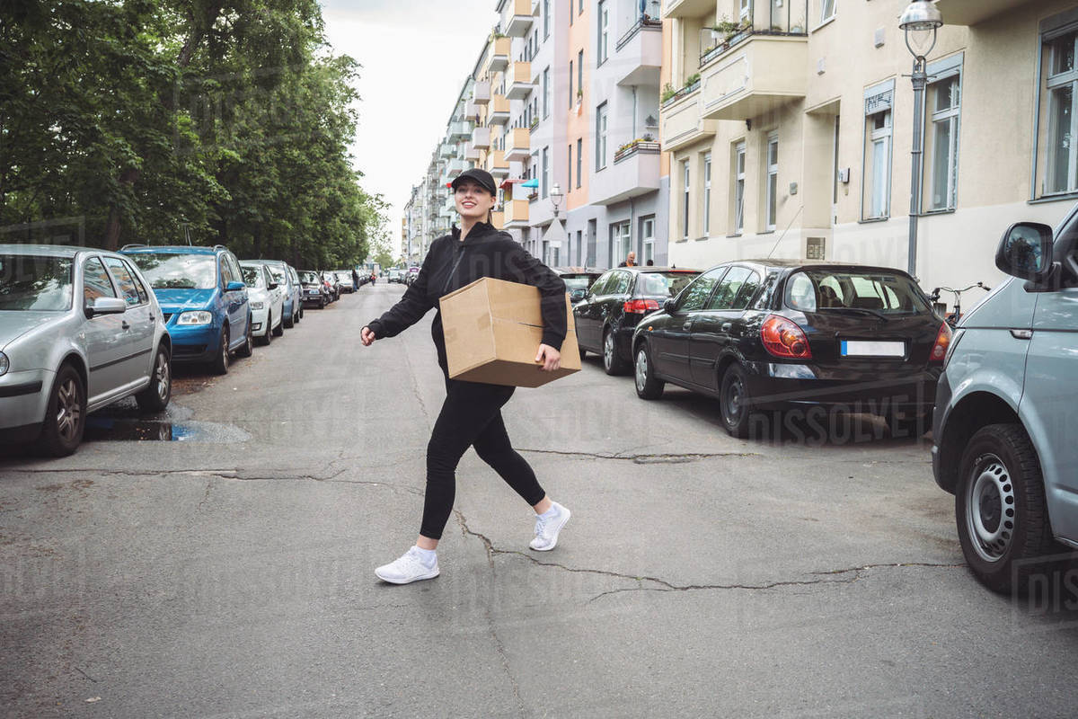 Confident delivery woman with cardboard box walking on street in city ...