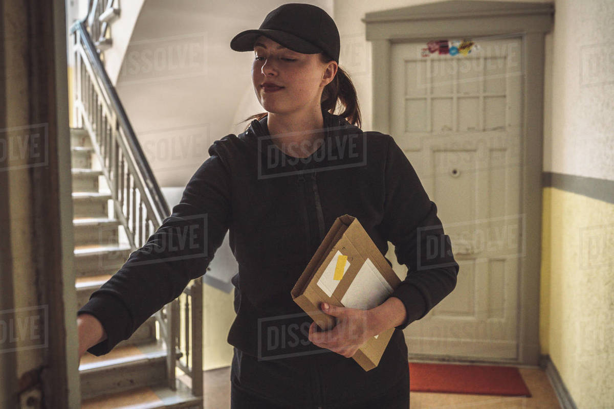 Confident delivery woman with package standing at doorstep - Stock ...