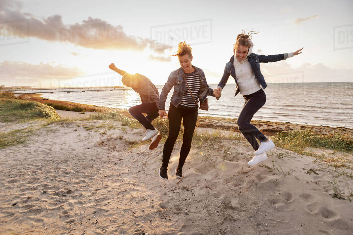 Smiling mother and children jumping at beach during weekend - Stock ...