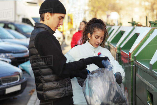 Side view of young male environmentalist with friend throwing plastic ...