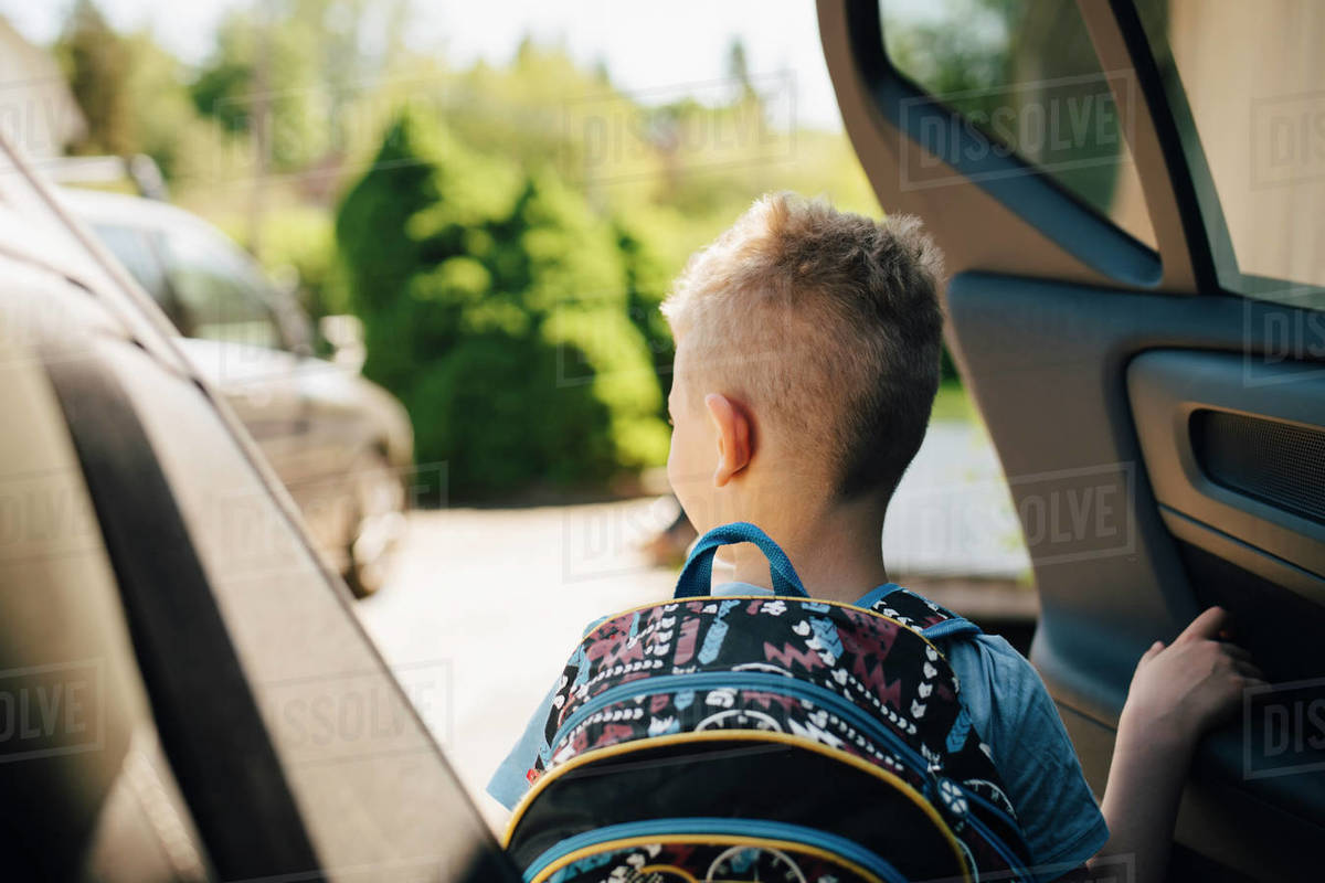 Rear view of boy with backpack opening car during sunny day - Stock ...