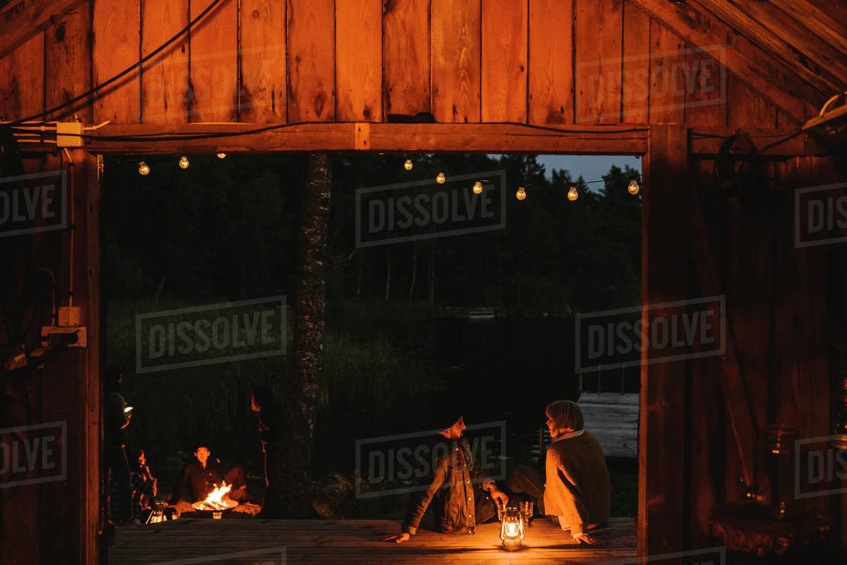Couple talking while friends sitting by fire pit during sunset ...