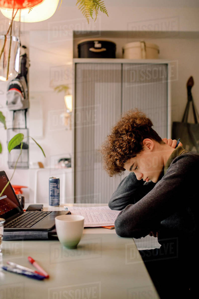 Tired boy reading book while studying at home - Stock Photo - Dissolve