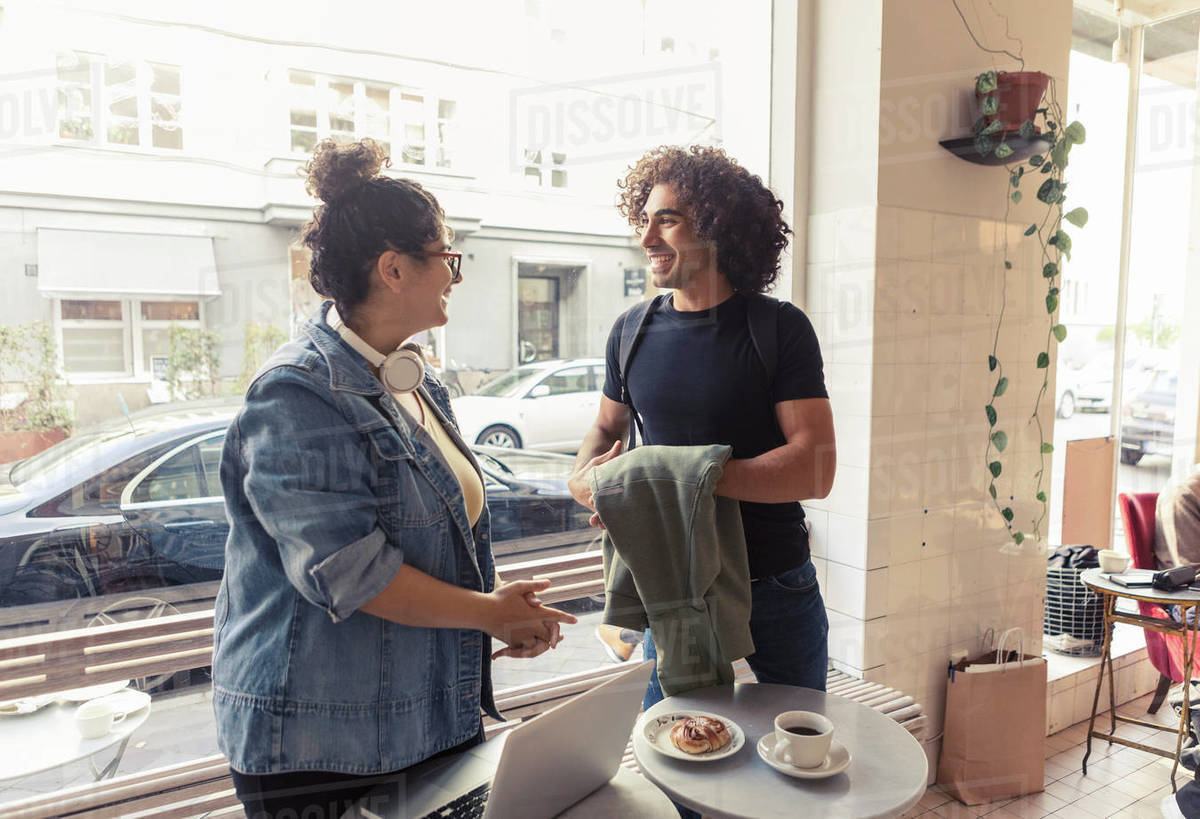 Happy male and female friends talking while standing at cafe - Royalty ...