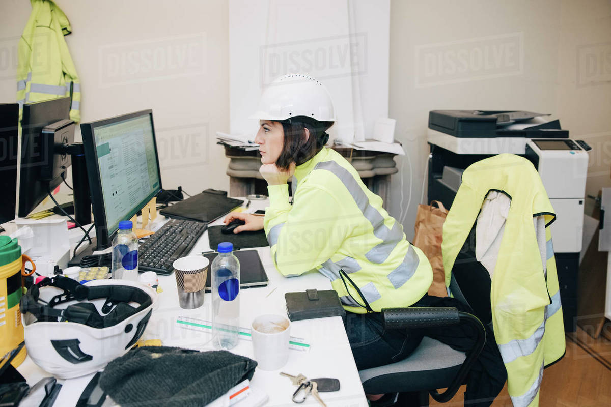 Side view of female engineer sitting with hand on chin while working on ...