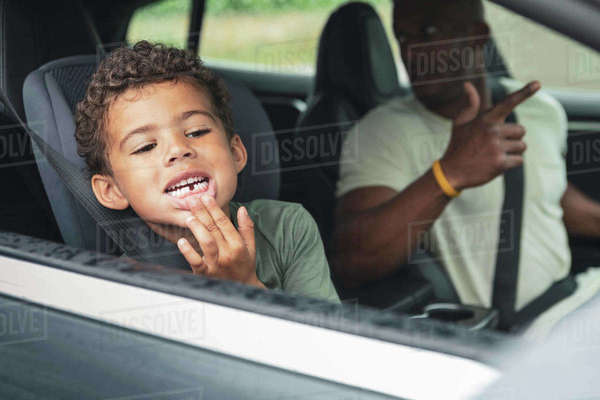 Playful boy showing broken teeth while sitting by father in electric ...