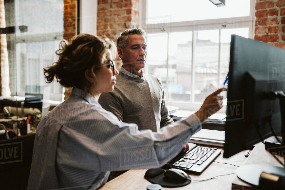 Female professional explaining businessman while pointing on computer ...
