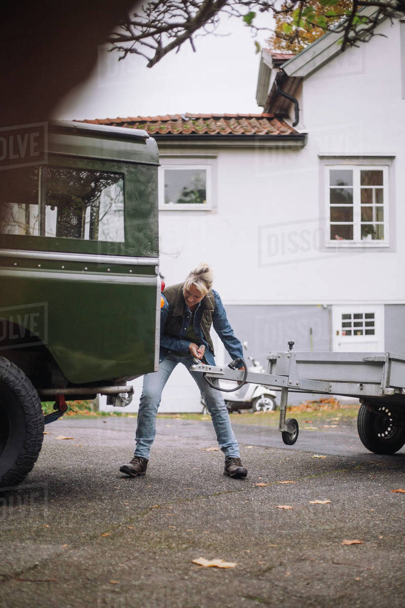 Mature woman towing trailer to sports utility vehicle on driveway ...