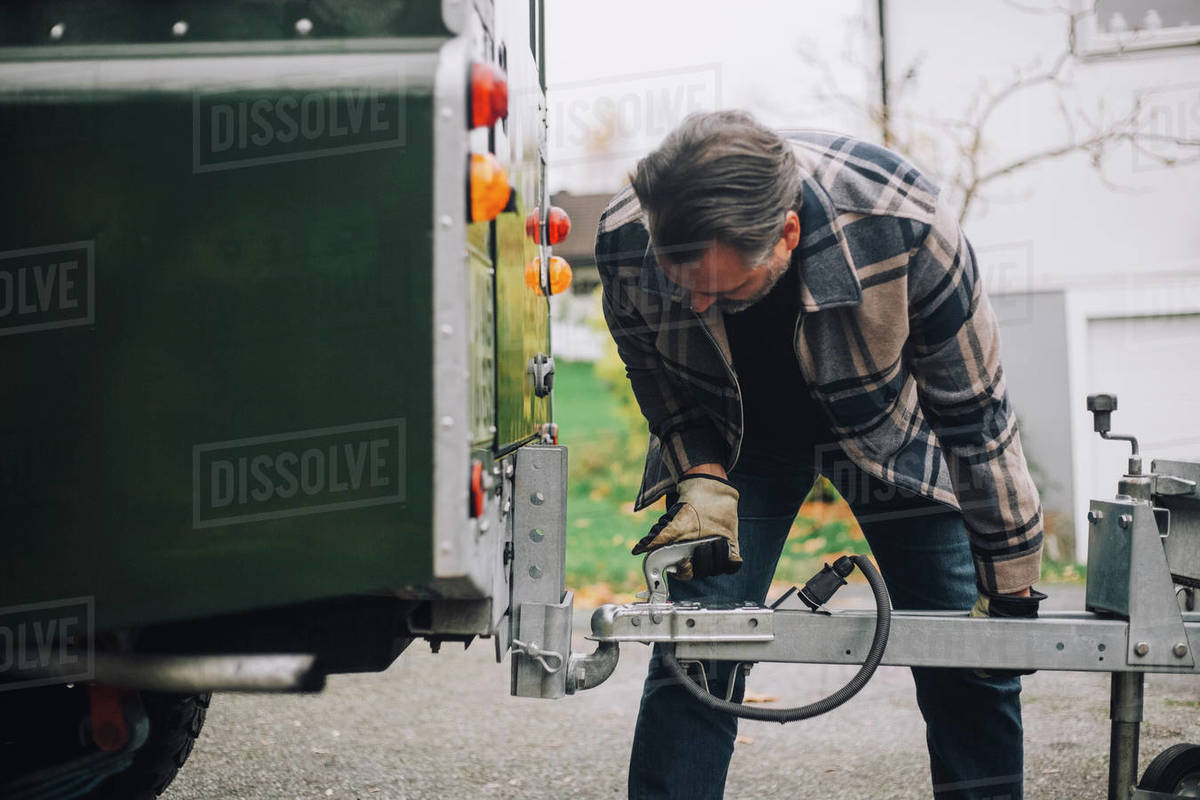 Mature man towing trailer to sports utility vehicle on driveway ...