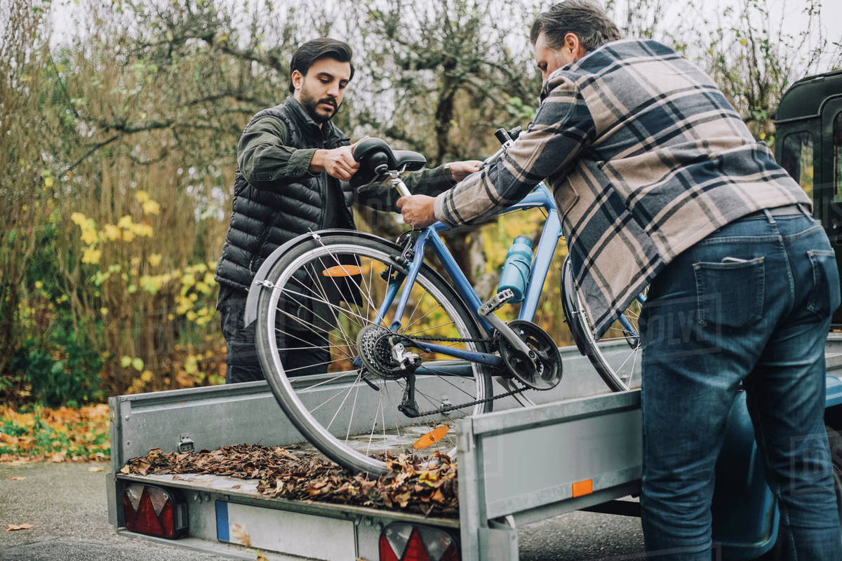 Son and father loading bicycle in vehicle trailer on driveway - Royalty ...