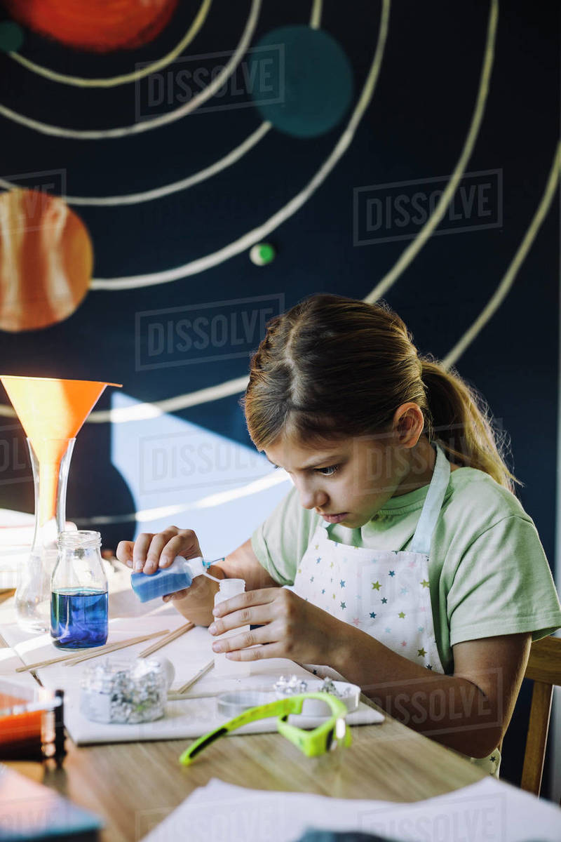 Focused girl pouring chemical while doing scientific experiment at home ...