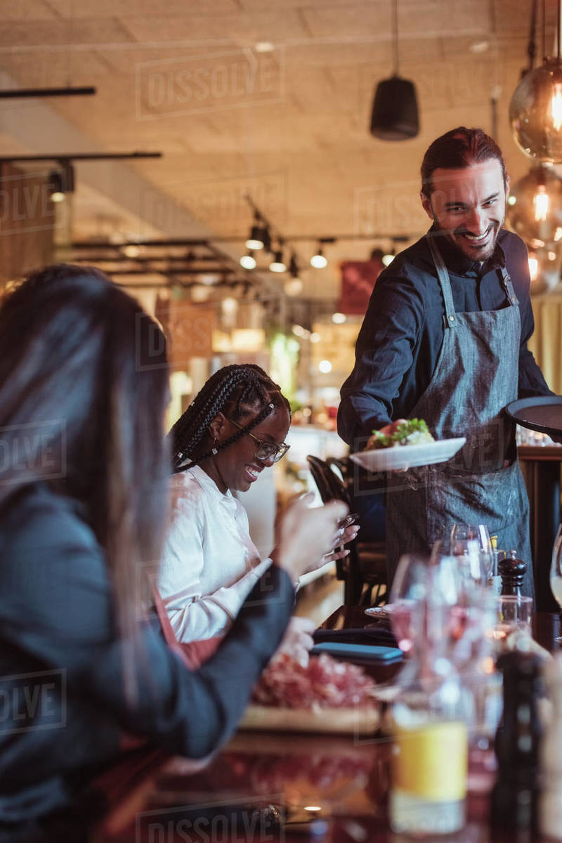 Happy waiter serving food to female customers in restaurant - Royalty ...