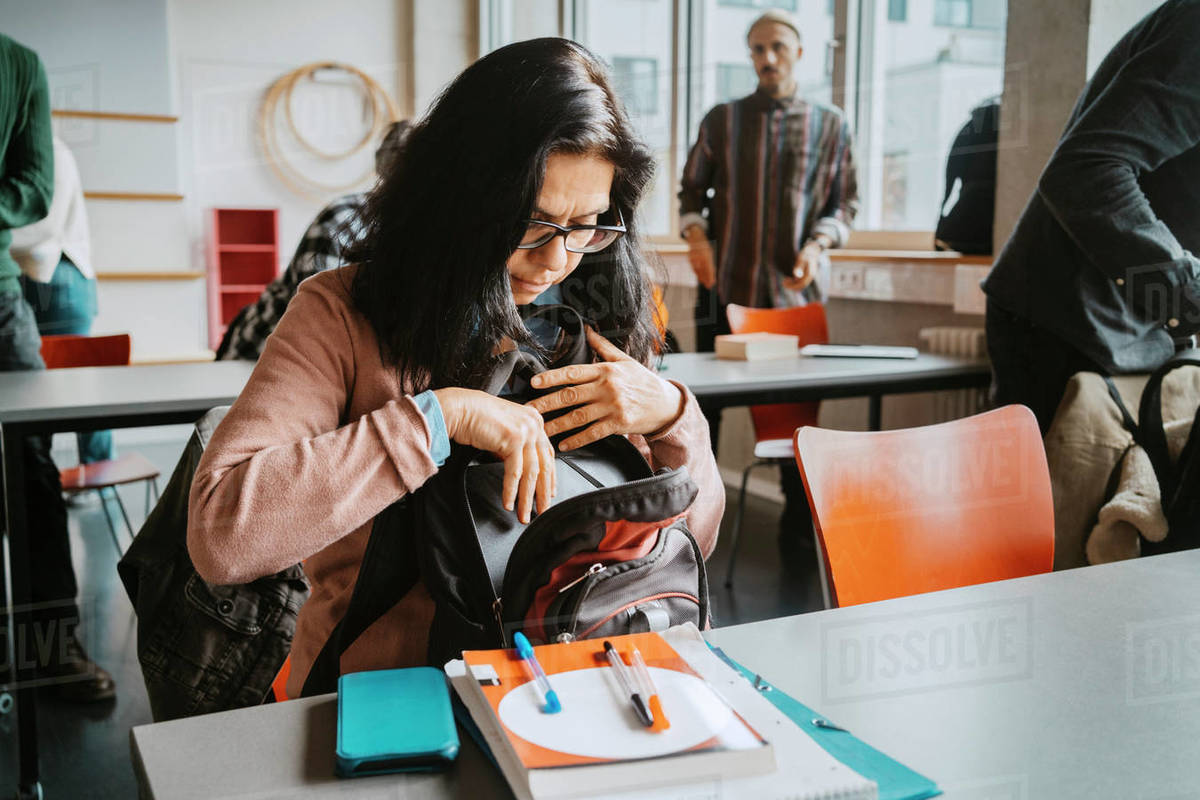 Mature female university student removing books from backpack while ...