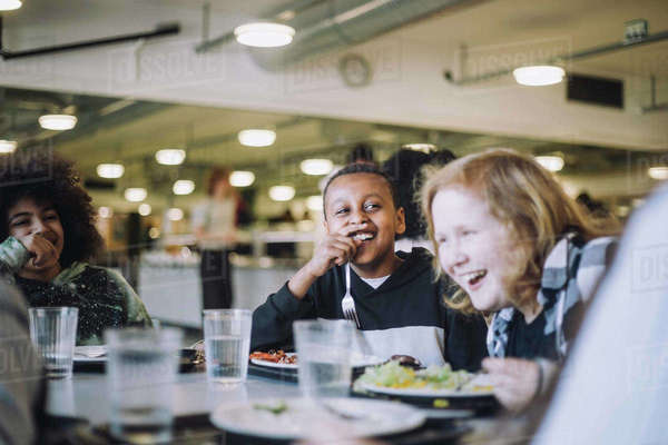 Friends laughing while having food at table during lunch break in ...