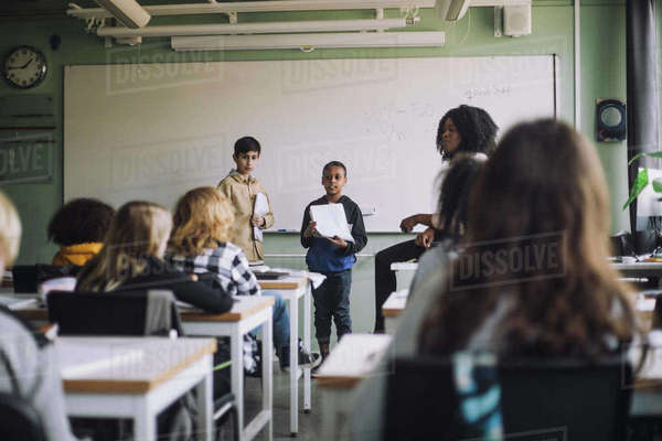 Boys holding reports while doing presentation to students in classroom ...