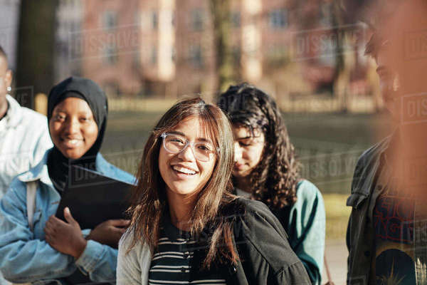 Portrait of smiling young female student with friends at university ...