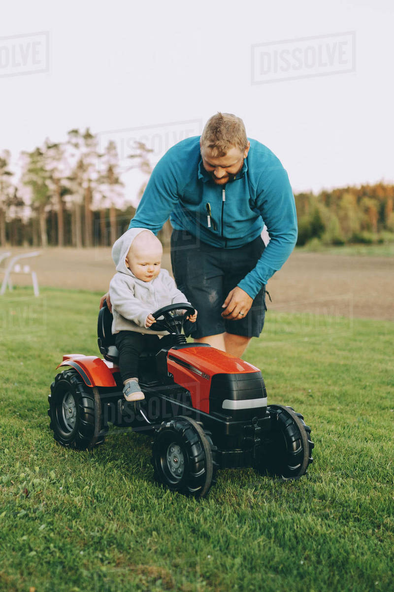 Father giving ride to son sitting in toy tractor at farm - Stock Photo ...