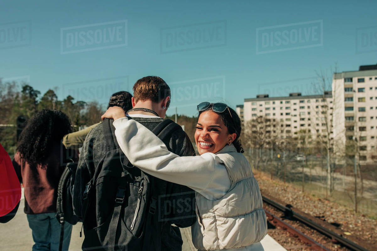 Happy woman looking over shoulder with arm around friend on sunny day ...