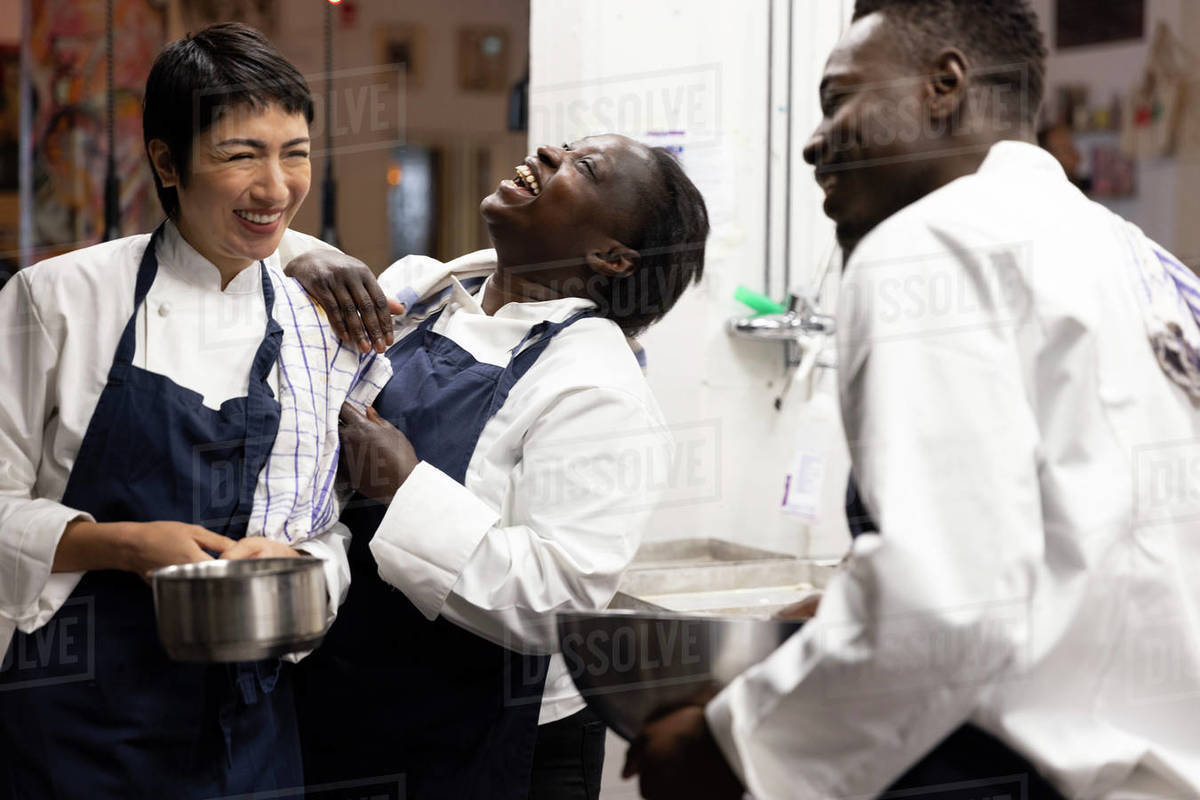 Multiracial chefs laughing while working in kitchen of restaurant ...
