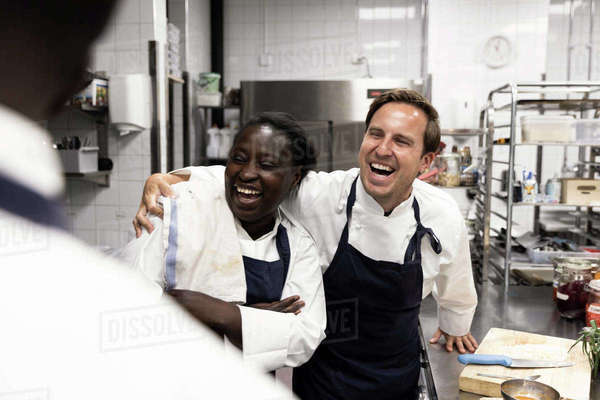 Happy chef with arm around female colleague in commercial kitchen ...