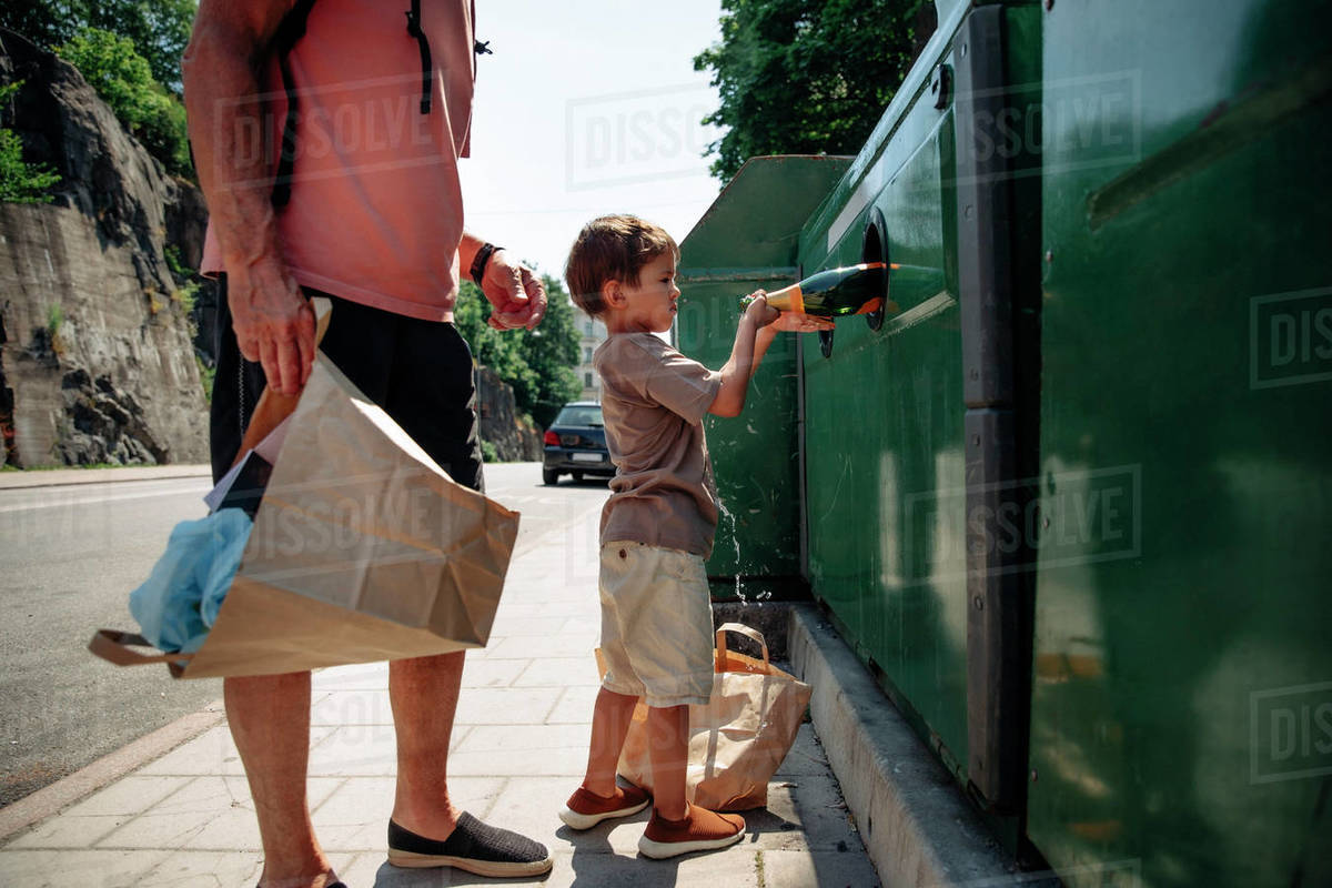Side view of boy trashing bottle in garbage bin while standing with ...