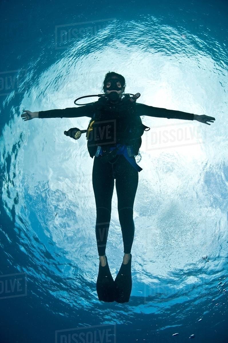 Full length front view of scuba diver arms open floating near water ...
