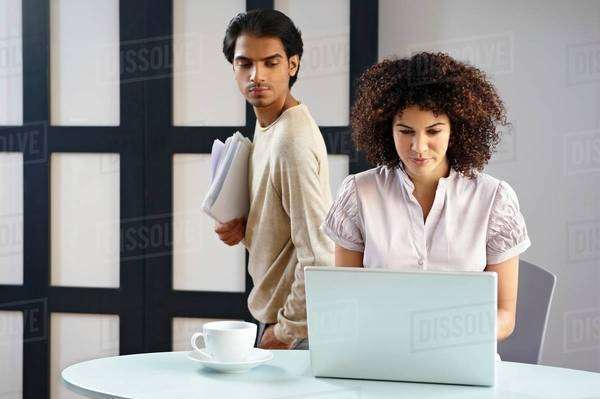 Man peering over woman's shoulder - Stock Photo - Dissolve