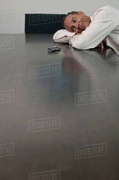 Man leaing on table looking at phone - Stock Photo - Dissolve