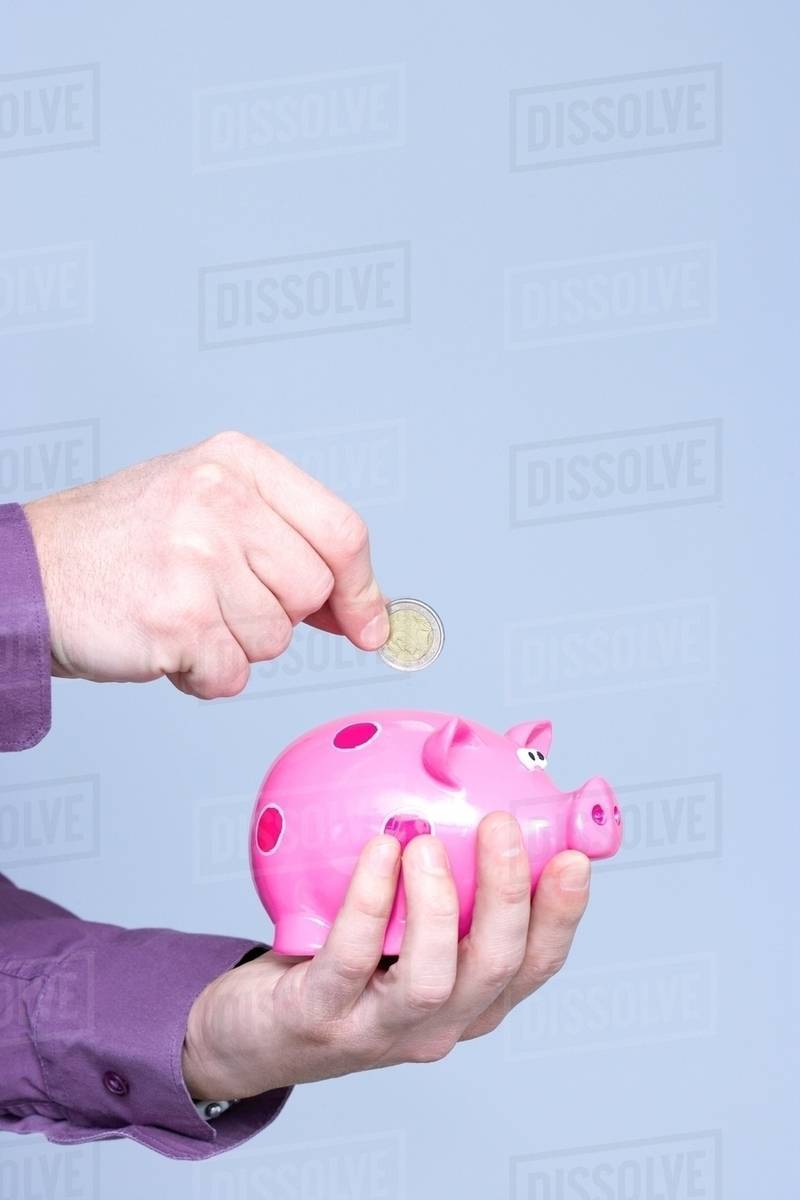 Hand dropping a coin in a piggy box - Royalty-free Stock Photo | Dissolve