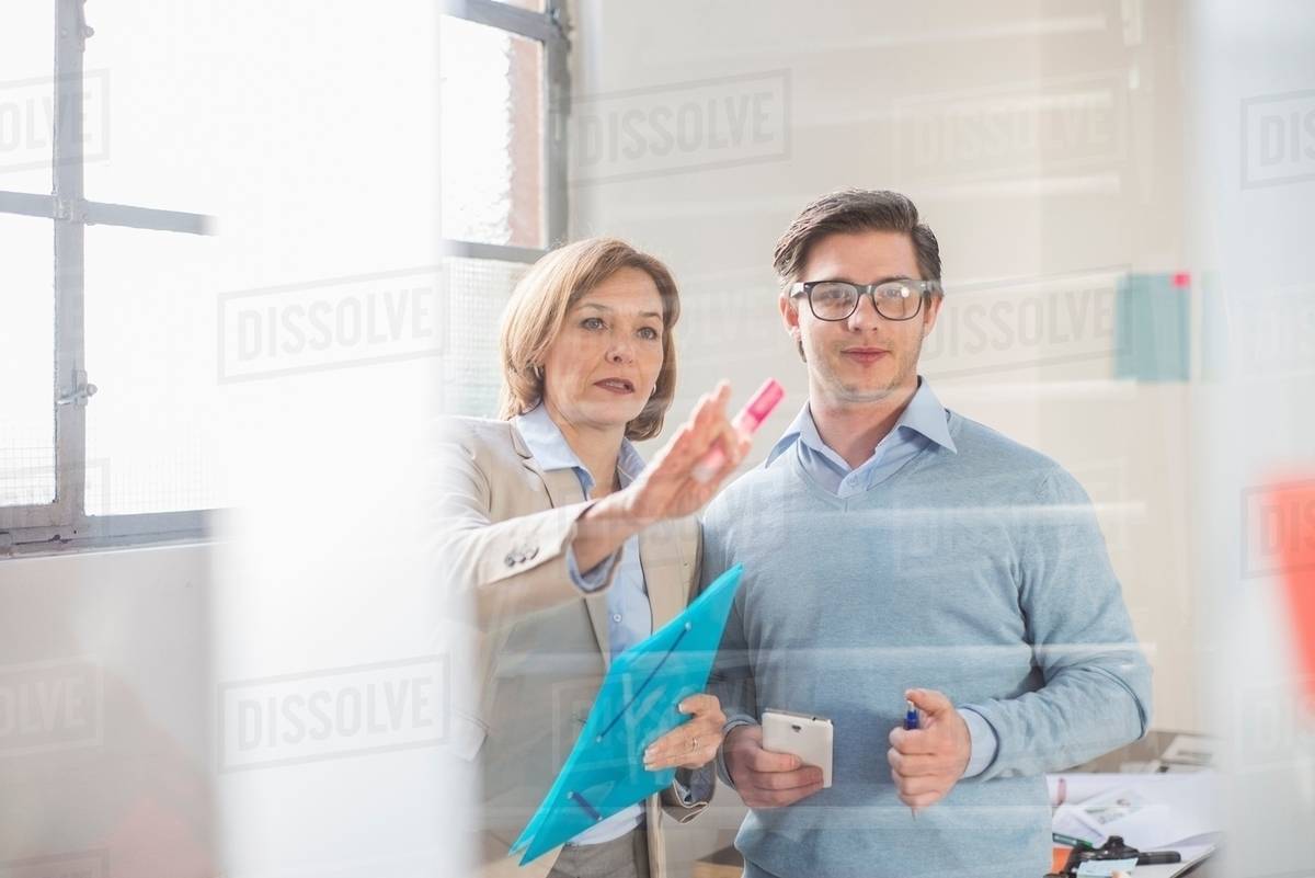 Businessman and woman pointing at office glass wall - Royalty-free ...